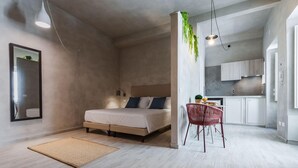 Quarto compacto com cama, mesa de cabeceira e um pequeno espaço de refeições com cadeira e mesa.