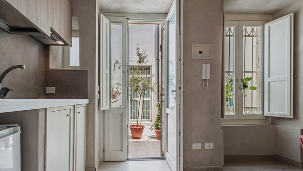 Um corredor estreito que leva a um solário com plantas em vasos e vista para o exterior.