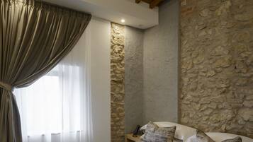 Quarto com parede de pedra, teto de madeira, cama com colcha estampada e mesa de cabeceira com telefone.
