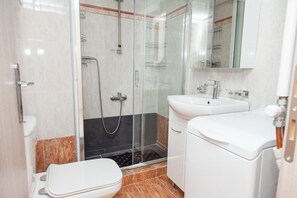 Uma casa de banho moderna com cabine de duche em vidro, lavatório branco e sanita.