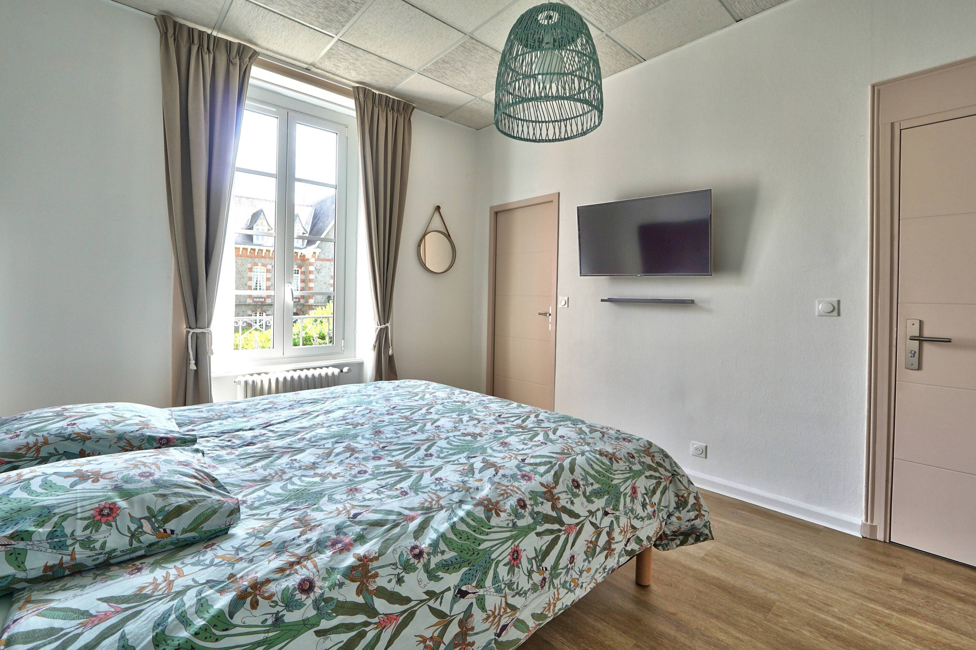 Quarto com cama, televisão, porta e janela com cortinas.