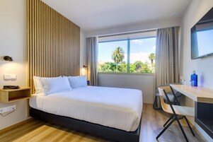 Quarto de hotel moderno com uma cama grande, uma escrivaninha e uma TV.