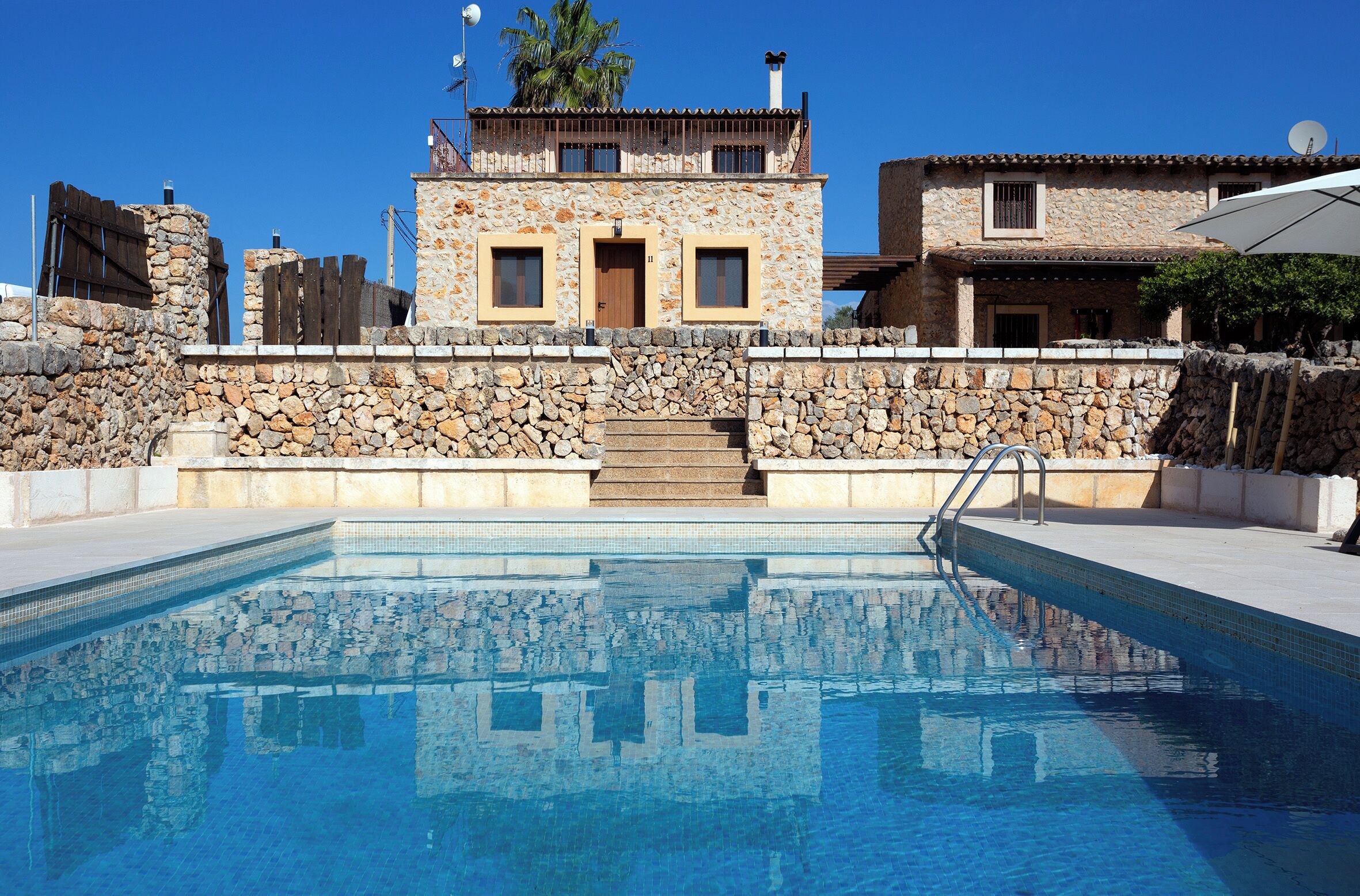 Piscina com paredes e escadaria de pedra, e um edifício com várias janelas e uma porta.