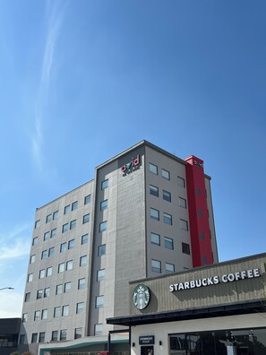 Um edifício moderno com um letreiro 'avid' em destaque no topo, uma placa da Starbucks Coffee abaixo e um céu azul claro ao fundo.