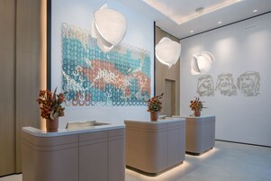 Uma área de recepção moderna com uma grande obra de arte abstrata na parede, dois balcões de atendimento e iluminação decorativa.