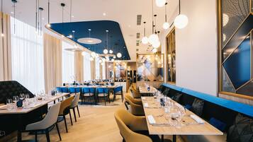 Um restaurante moderno com mesas comunitárias compridas, cabines individuais e luminárias pendentes.