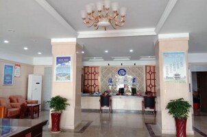 Um hall de hotel com balcão de recepção, área de estar e plantas decorativas.