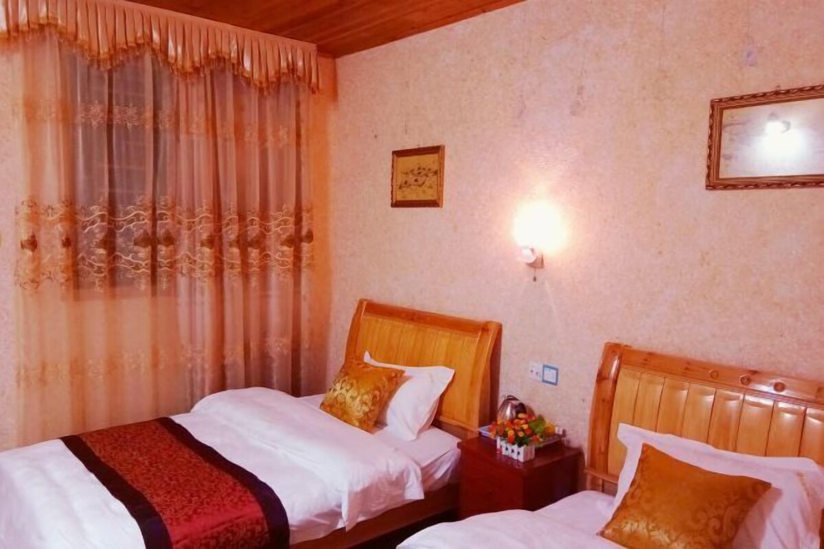Quarto de hotel com duas camas de madeira, uma mesa de cabeceira com abajur e um quadro na parede.