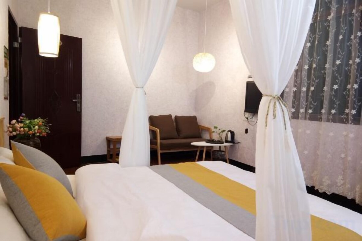 Quarto de hotel com cama, mesa pequena, sofá e cortina.