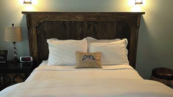 Uma cama bem arrumada com lençóis brancos e um travesseiro decorativo, com duas luminárias fixadas na parede.