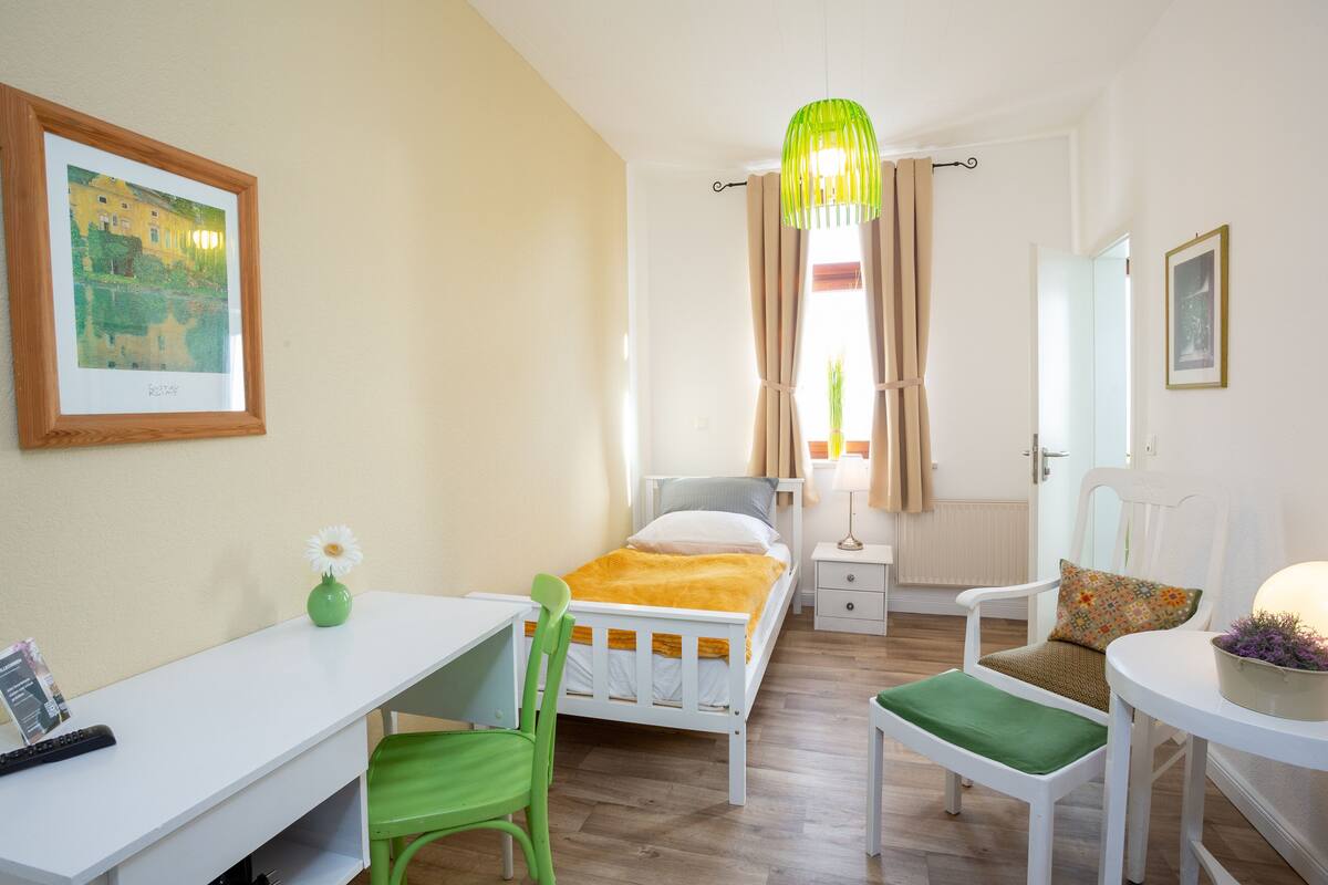 Quarto com cama, escrivaninha, cadeira, mesa de cabeceira e luminária suspensa.