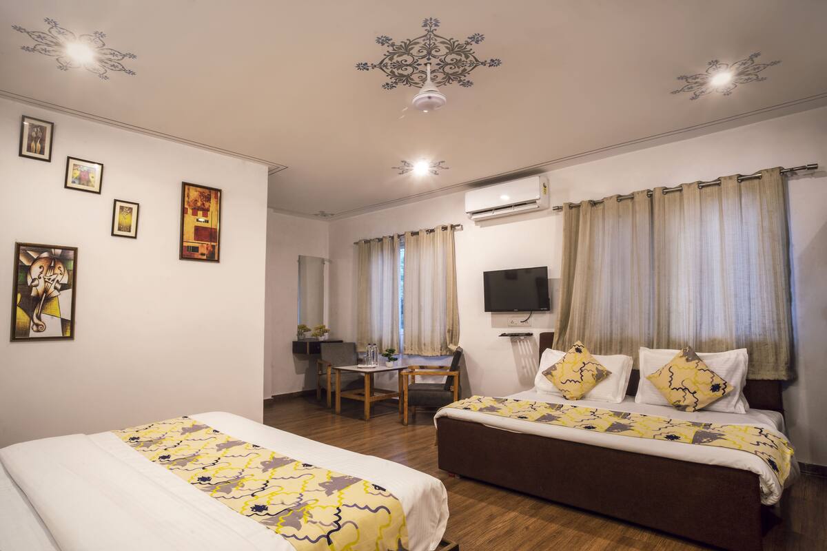 Quarto de hotel com duas camas, uma televisão, aparelho de ar condicionado e uma mesa com cadeira.