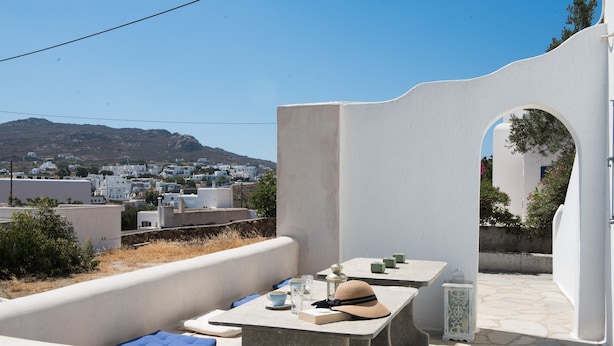 Terraço com mesa posta para dois, com vista para uma cidade de edifícios brancos e uma montanha ao fundo.