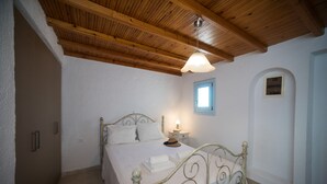 Quarto com teto de madeira, cama com roupa de cama branca, mesa de cabeceira com luminária e uma pequena janela.