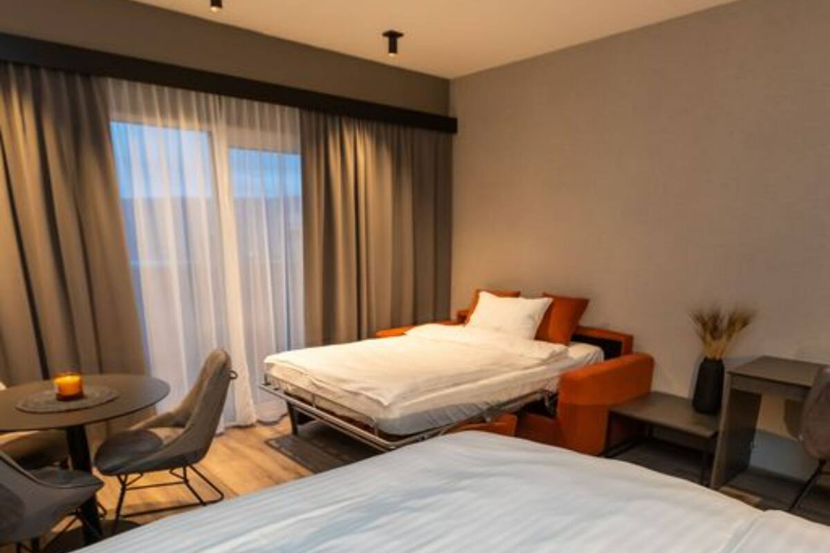 Quarto de hotel com uma cama grande, mesa de cabeceira, cadeira, pequena mesa com uma vela e janela com cortinas.
