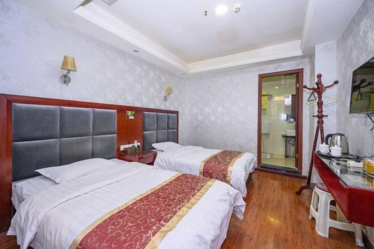 Quarto de hotel com duas camas, cabeceira de madeira, escrivaninha com cadeira e espelho.