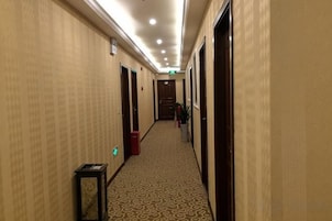 Corredor de hotel com portas em ambos os lados, carpete estampado e uma lixeira.