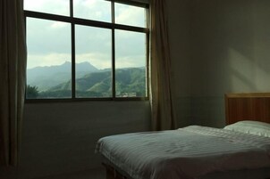 Quarto com uma janela grande que oferece vista para colinas verdes e montanhas.