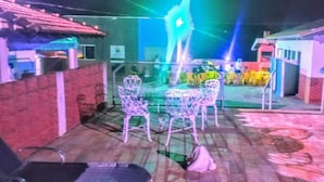 Uma área de estar ao ar livre com piscina, cadeiras brancas e uma mesa.