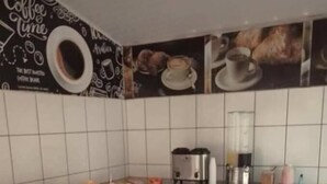 Uma sala de jantar com uma mesa posta para dois, uma cafeteira e prateleiras com utensílios de cozinha.