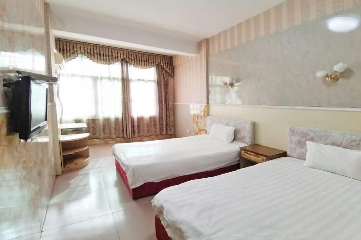 Quarto de hotel com duas camas, televisão, secretária e janela com cortinas.
