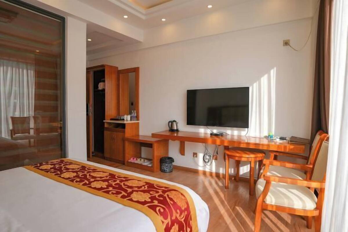 Quarto de hotel com cama, escrivaninha, televisão e guarda-roupa.