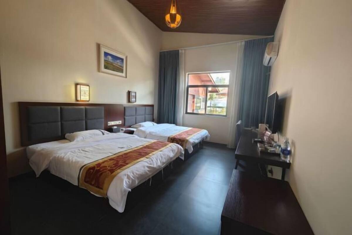 Quarto de hotel com duas camas, uma escrivaninha, televisão e janela com cortinas.