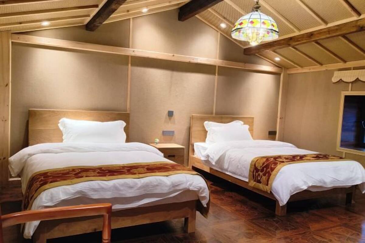 Quarto com duas camas de madeira, uma cadeira de madeira e um lustre.