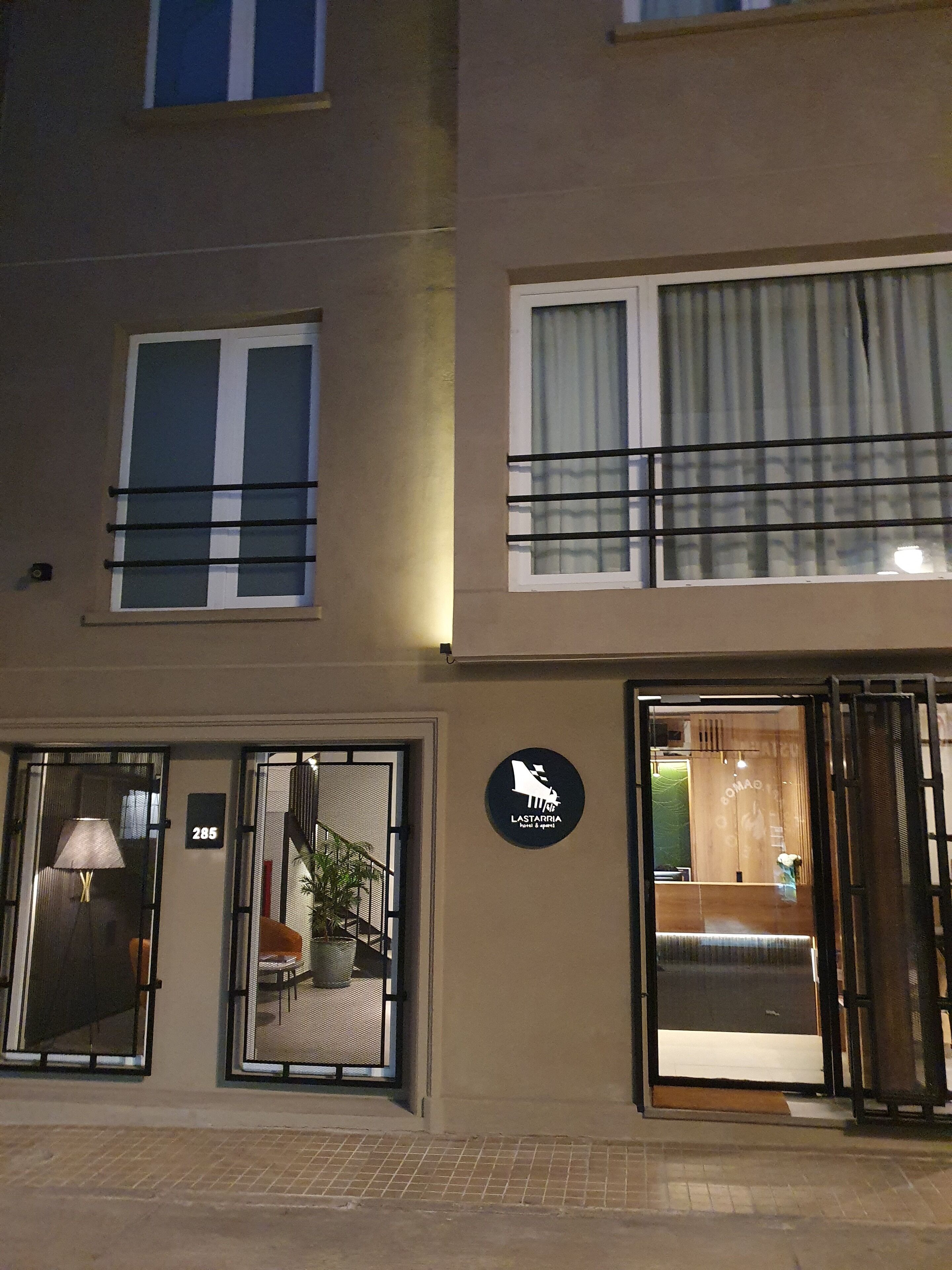 Entrada de hotel com placa, escadas e vista do interior através das portas de vidro.