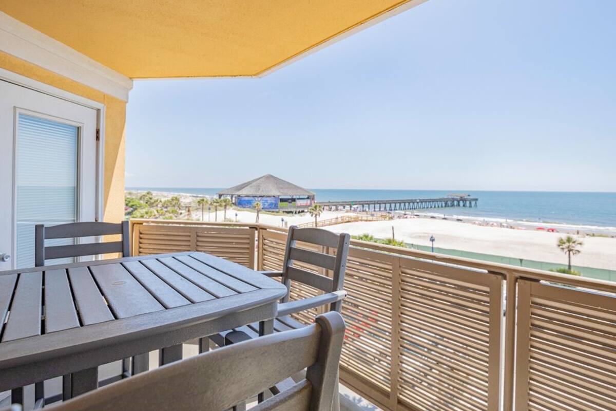 Varanda com mesa e cadeiras com vista para uma praia e um cais.