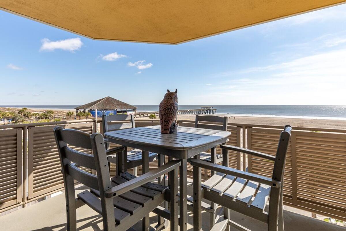 Um pátio com mesa e cadeiras, com vista para a praia.