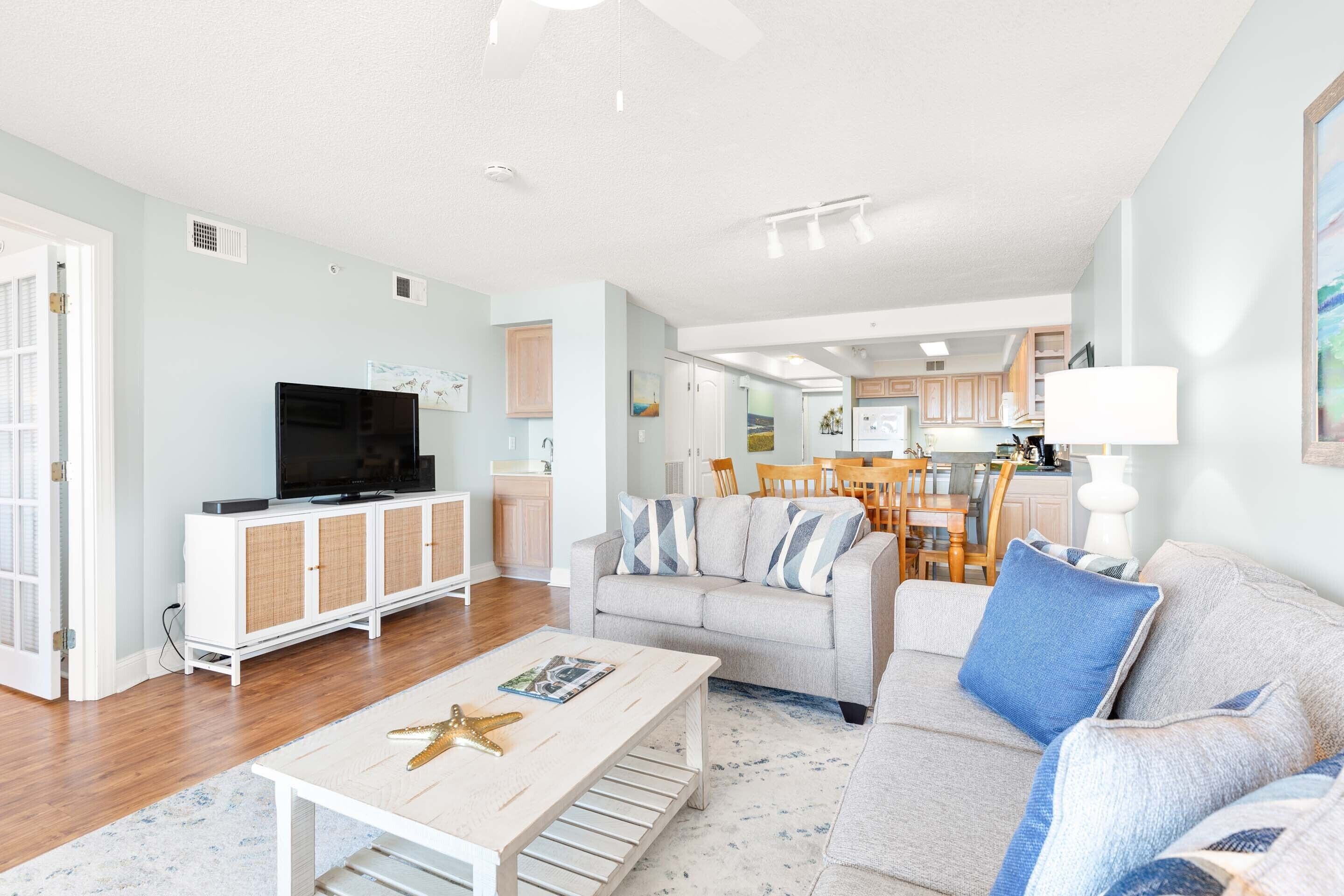 Uma sala de estar moderna com uma TV de tela plana, um móvel branco para aparelhos eletrônicos, um sofá cinza e uma mesa de centro com uma decoração de estrela-do-mar.
