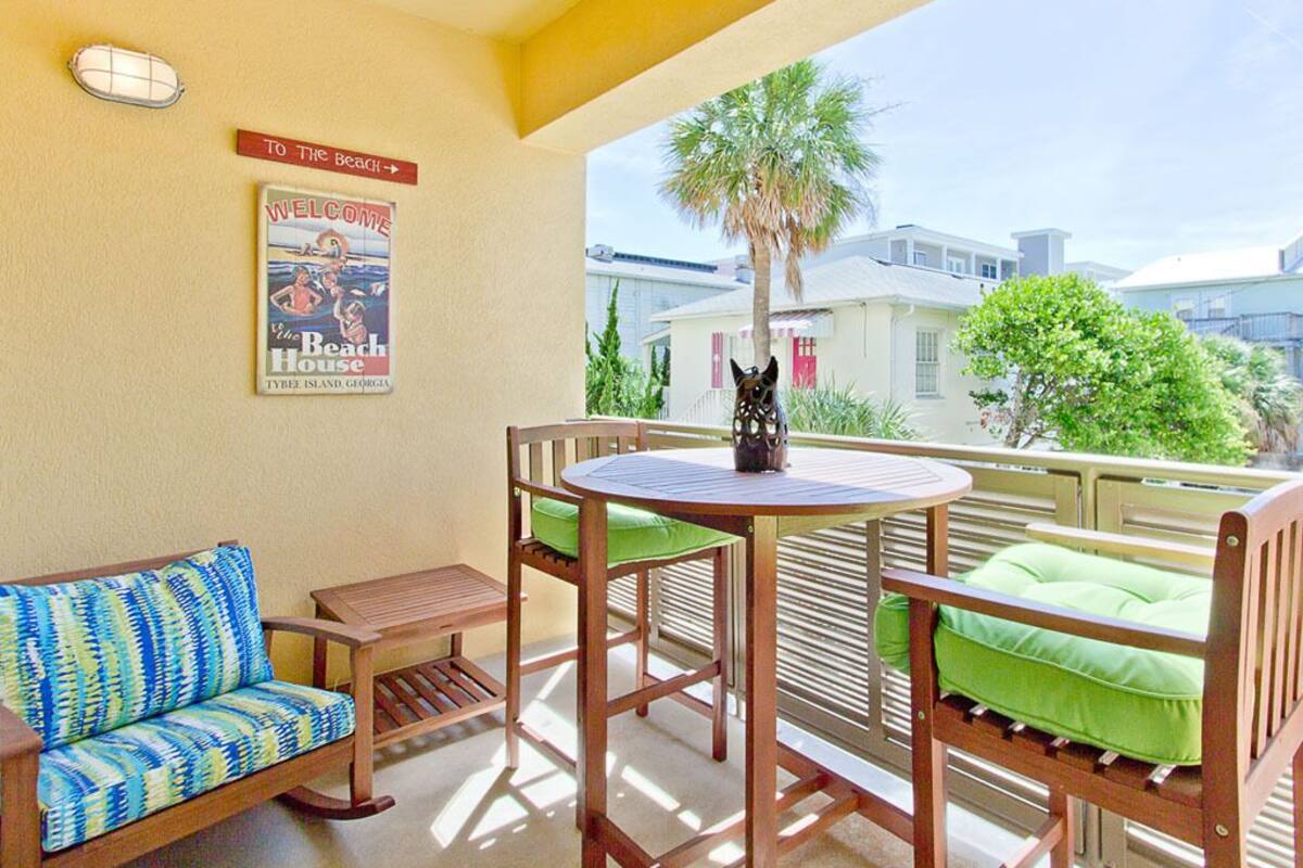 Uma varanda com mesa e cadeiras de madeira, um sofá e um quadro na parede.