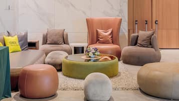 Uma área de estar moderna com sofá, pufes, mesa de centro redonda e uma pequena mesa lateral.
