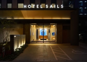 A entrada de um hotel com design moderno, com uma porta de vidro e uma placa acima que diz "HOTEL SAILS".