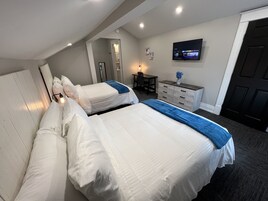 Quarto de hotel com duas camas, uma escrivaninha, uma cadeira, uma cômoda, uma TV e uma porta.