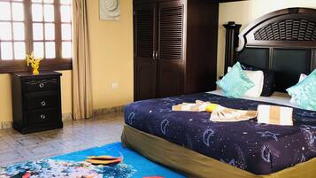 Quarto com cama, ventoinha no teto, janela com cortinas e mesa de cabeceira com abajur.