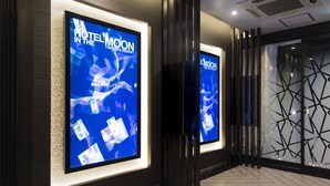 Um hall de hotel moderno com telas digitais exibindo 'Hotel Moon in the Timeless Resort' e uma parede com padrão geométrico.