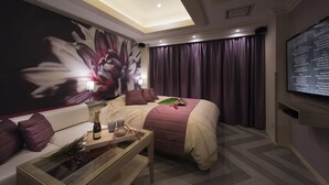 Quarto de hotel moderno com uma cama grande, televisão de tela plana, iluminação no teto e um mural floral na parede.