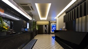 Um hall de hotel moderno com uma mesa de recepção, uma tela digital e uma área de estar.