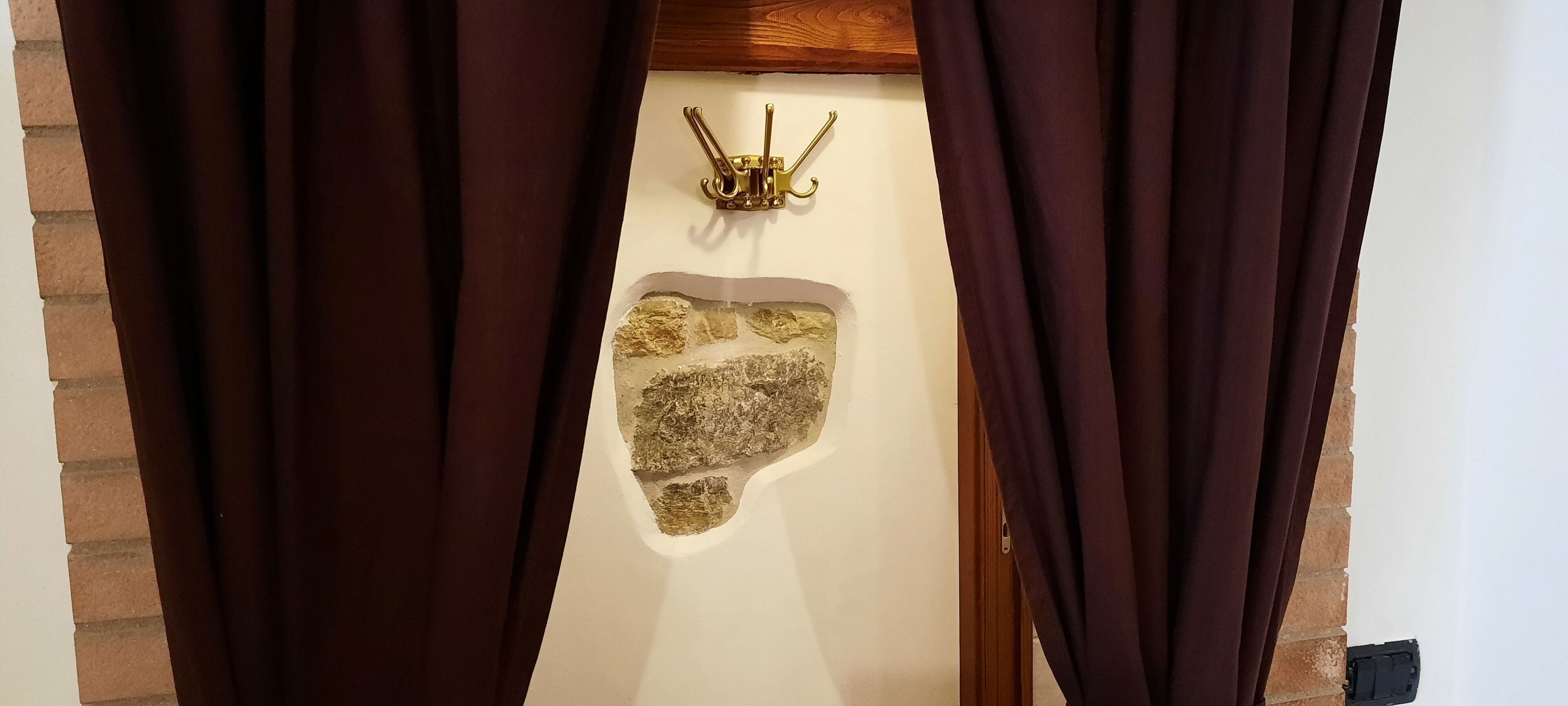Uma porta com parede de pedra, um porta-roupas de metal e cortinas escuras.