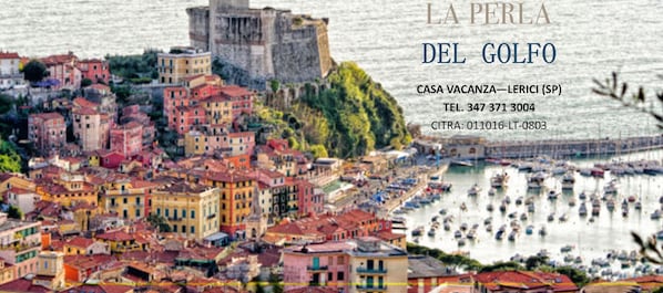 Uma vila costeira com edifícios coloridos, um castelo e barcos na água.