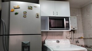 Uma cozinha compacta com geladeira de aço inoxidável, micro-ondas e máquina de lavar.
