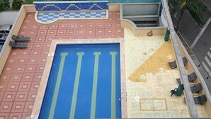 Piscina no terraço com chão de azulejos azuis e vermelhos, rodeada por espreguiçadeiras e uma pequena área de estar.