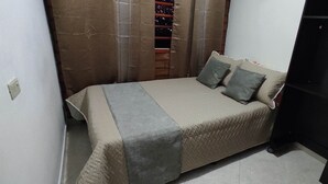 Um quarto pequeno com uma cama, um guarda-roupa e uma cortina.