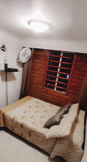 Quarto pequeno com cama, janela com grades, ventilador de teto e sinal de Wi-Fi.