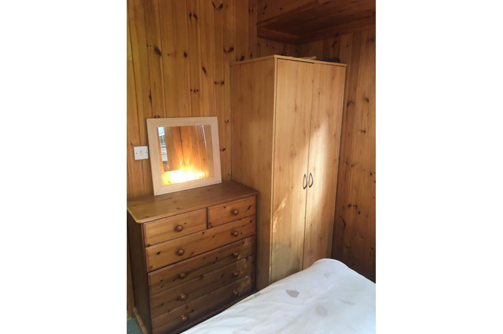 Quarto de madeira com cama, cômoda e guarda-roupa.