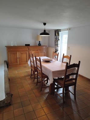 Uma sala de jantar com uma mesa posta para quatro, cadeiras de madeira, um armário, um abajur e uma janela com cortinas.