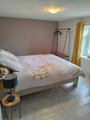 Quarto com cama, mesa de cabeceira com abajur, cadeira suspensa e janela com cortinas.