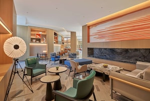 Um hall de hotel moderno com áreas de estar, uma mesa de recepção e uma grande obra de arte abstrata na parede.